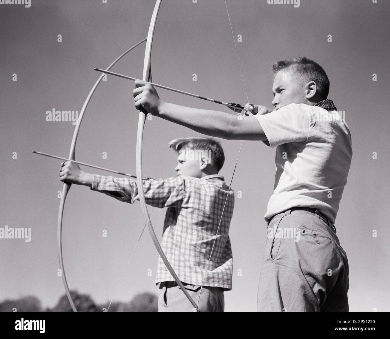 1950s TWO PRETEEN BOYS ARCHERS AIMING SHOOTING BOWS AND ARROWS TOGETHER ...