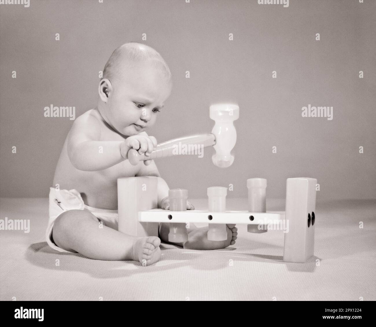1960s BABY BOY SITTING WITH TOY PLASTIC HAMMER POUNDING PLASTIC NAILS ...