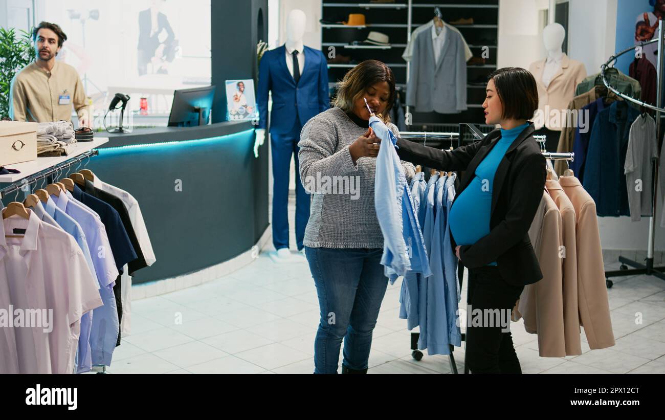 Female client with baby bump shopping for formal wear in clothing store ...