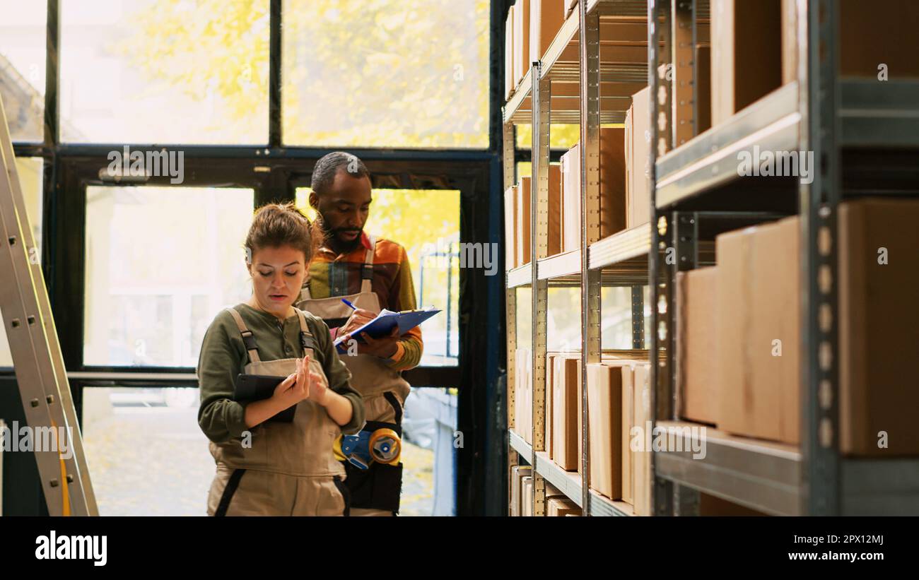 Diverse people examining production in warehouse using inventory list ...