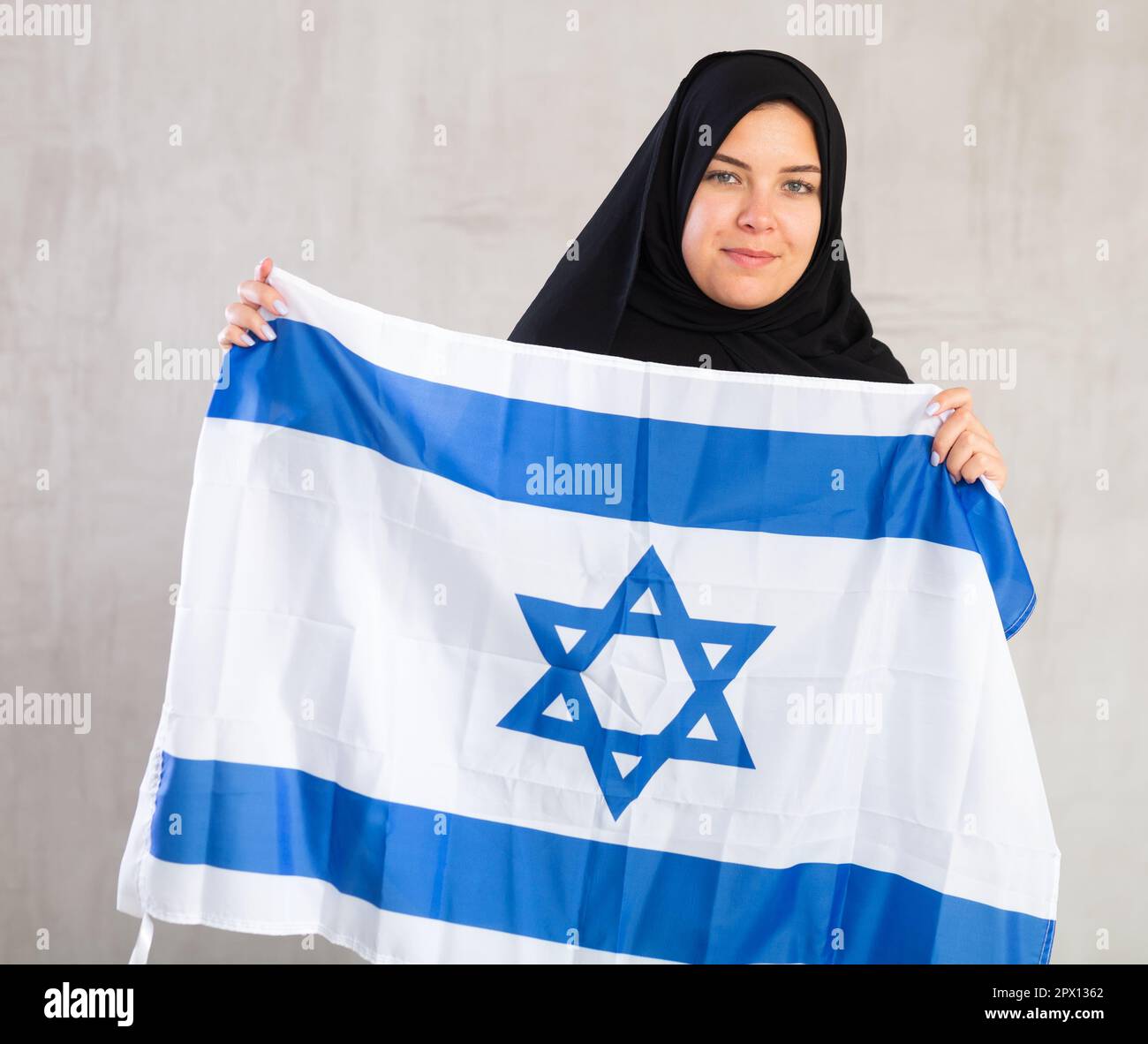 Balanced smiling Muslim woman in traditional black hijab holds flag of ...