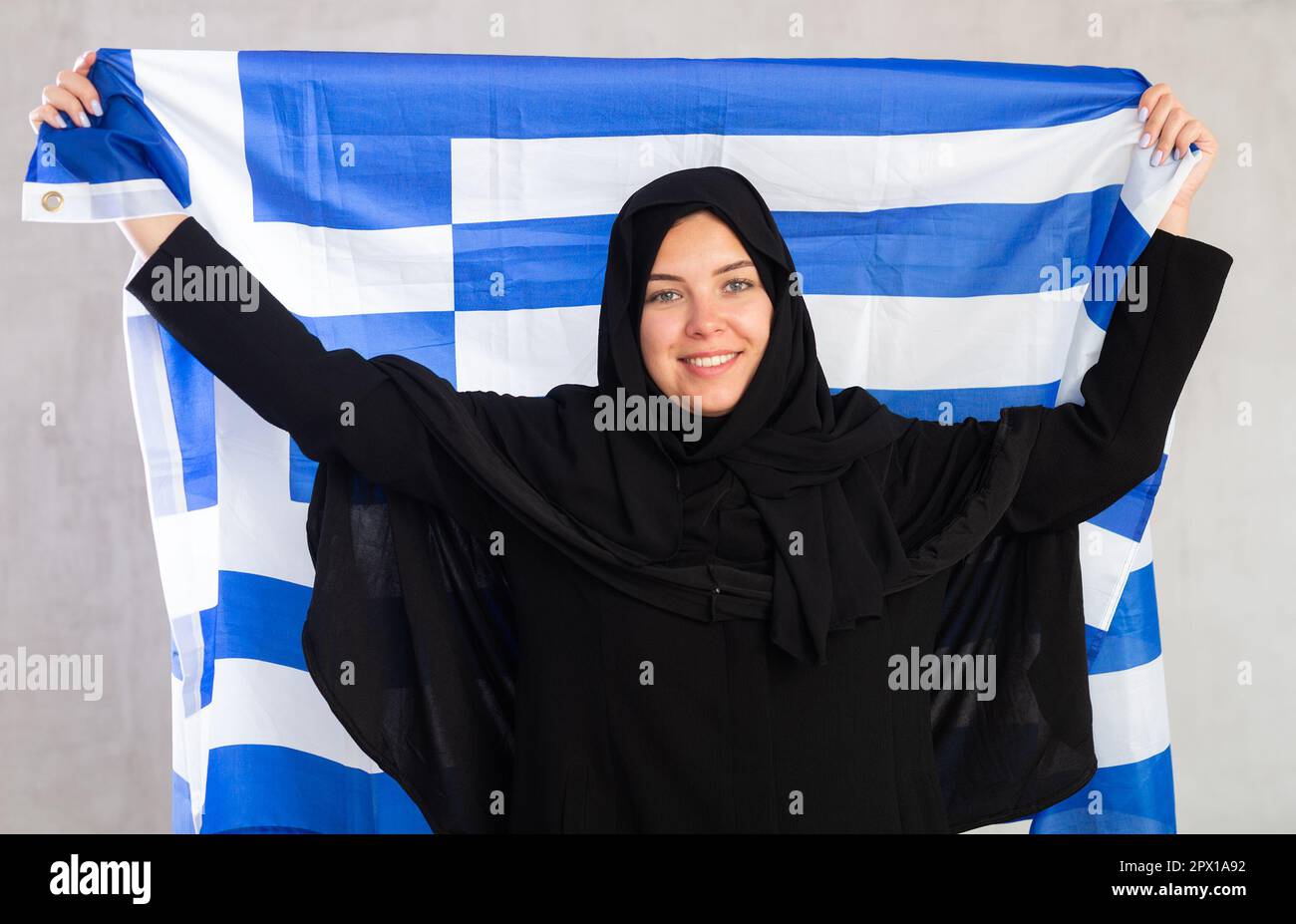 Balanced smiling Muslim woman in traditional black hijab holds flag of ...