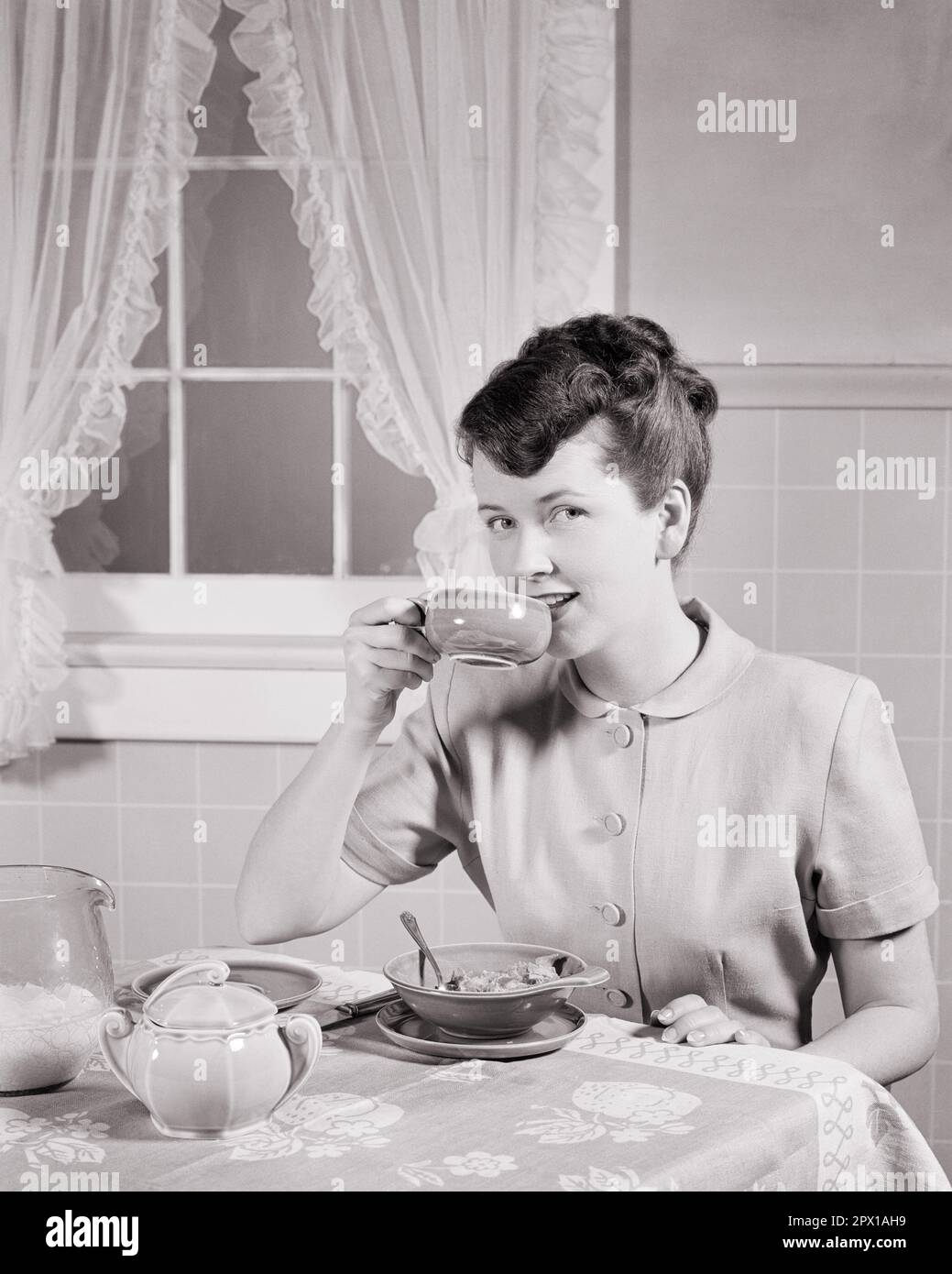 1950s WOMAN SITTING AT BREAKFAST TABLE SET WITH BOWL OF CEREAL DRINKING ...