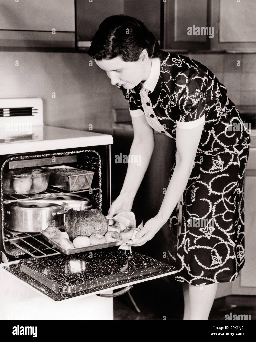 1930s BRUNETTE HOUSEWIFE TAKING A ROAST OUT OF THE OVEN THAT IS STUFFED ...