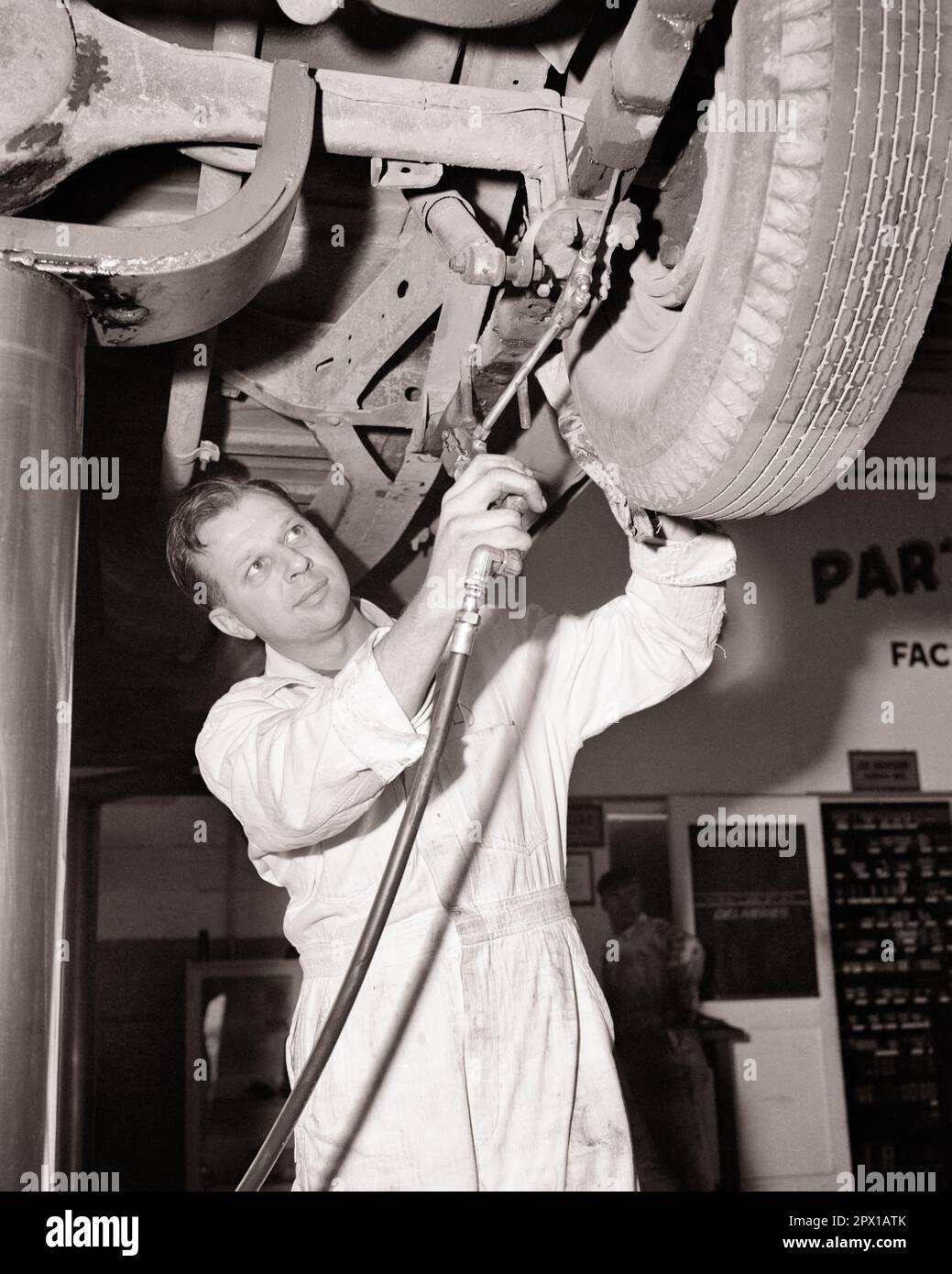 1950s MAN GARAGE MECHANIC WEARING WHITE COVERALLS WORKING LUBRICATING ...