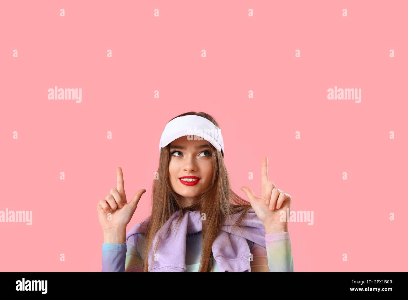 Stylish young woman in cap pointing at something on pink background ...