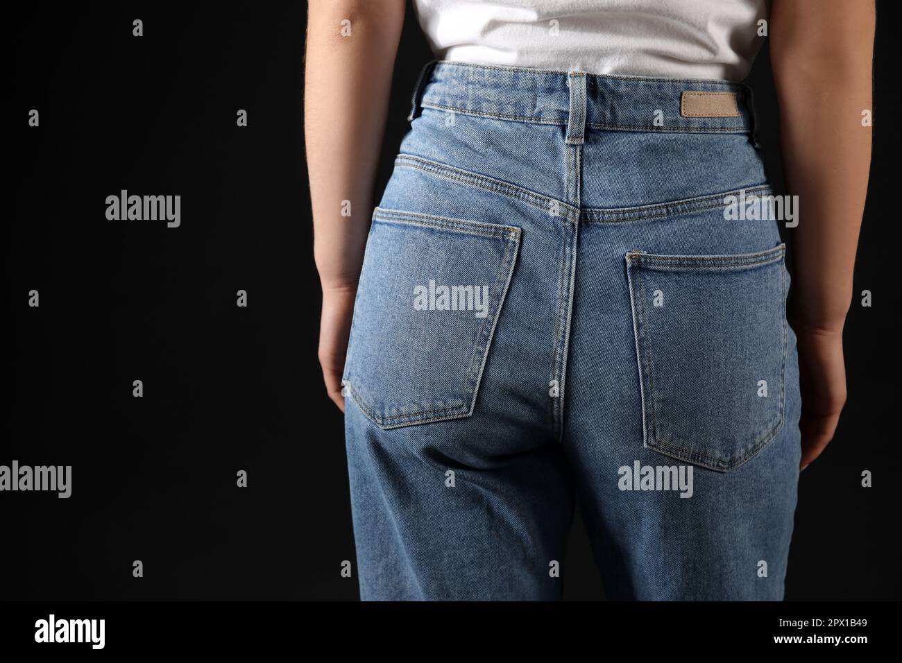 Young woman in stylish jeans on black background, back view Stock Photo ...