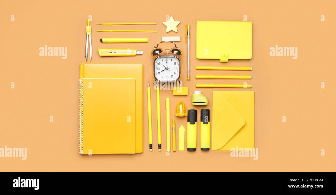 Set of yellow school supplies with alarm clock on brown background ...