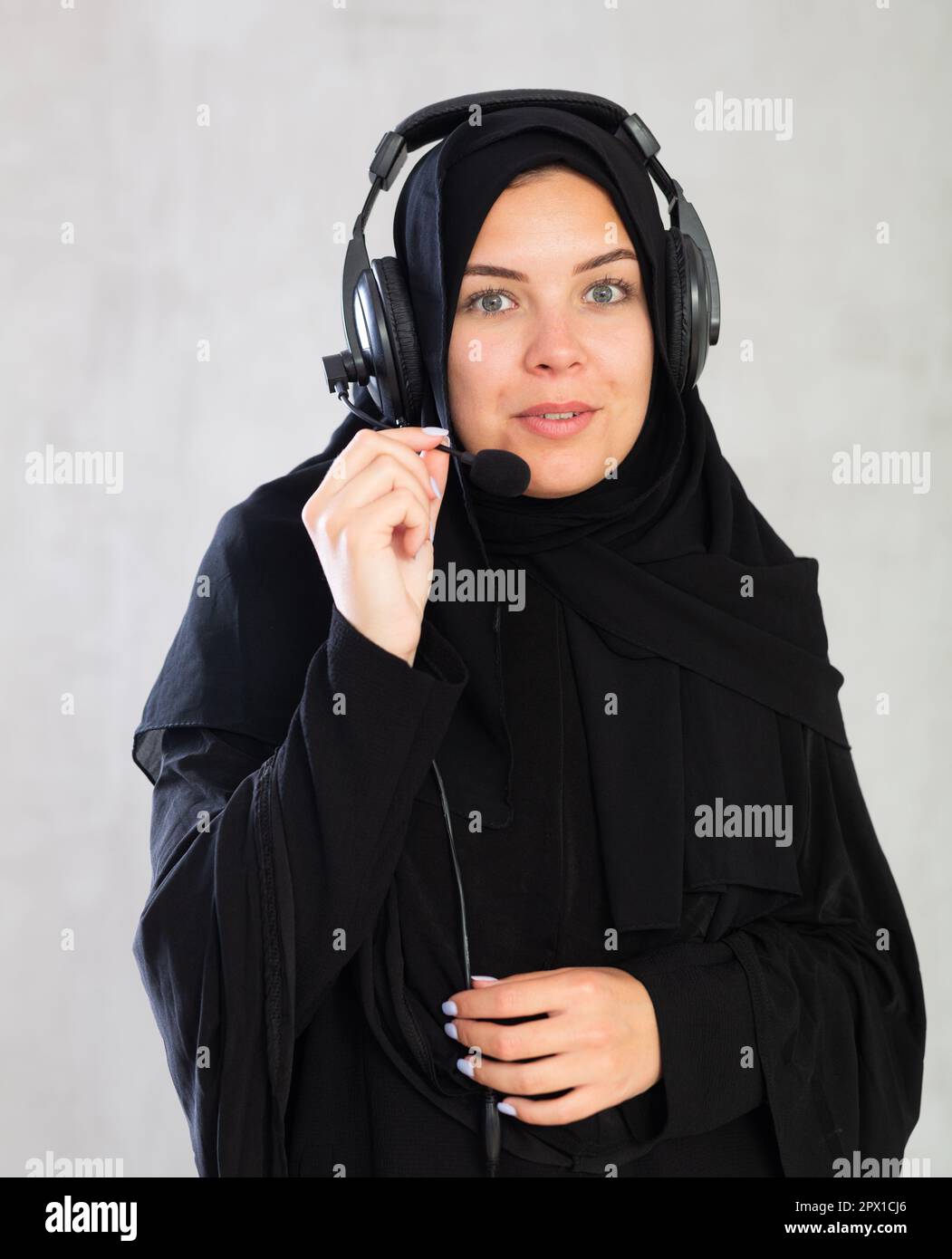 smiling Muslim woman in black hijab and headphones with microphone on ...