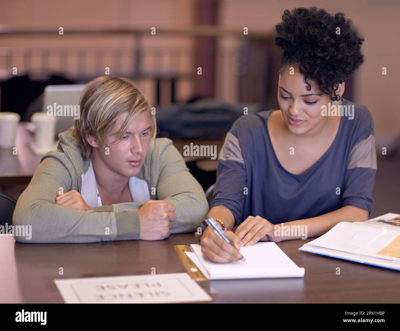 Lending a helping hand. Two students working together and writing notes ...