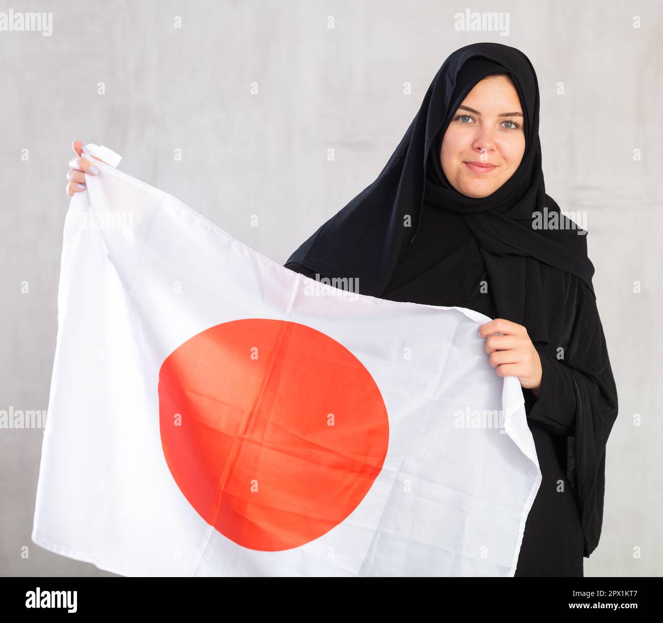 Balanced Muslim woman in traditional black hijab holds flag of Japan ...