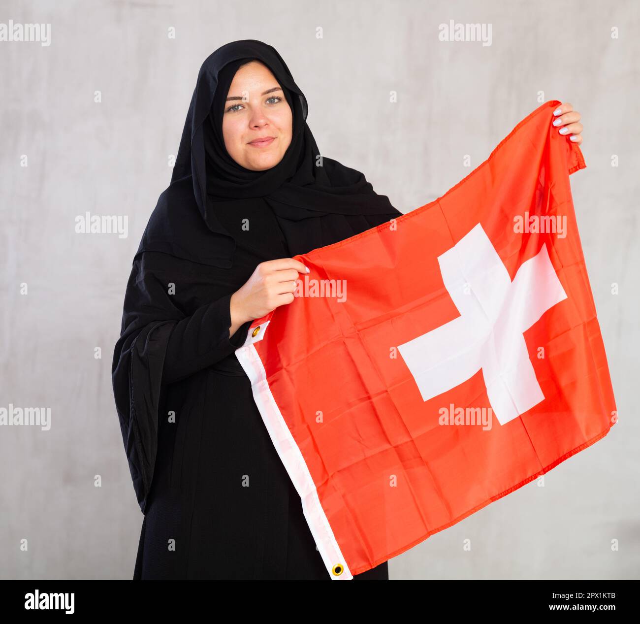 Balanced smiling Muslim woman in traditional black hijab holds flag of ...