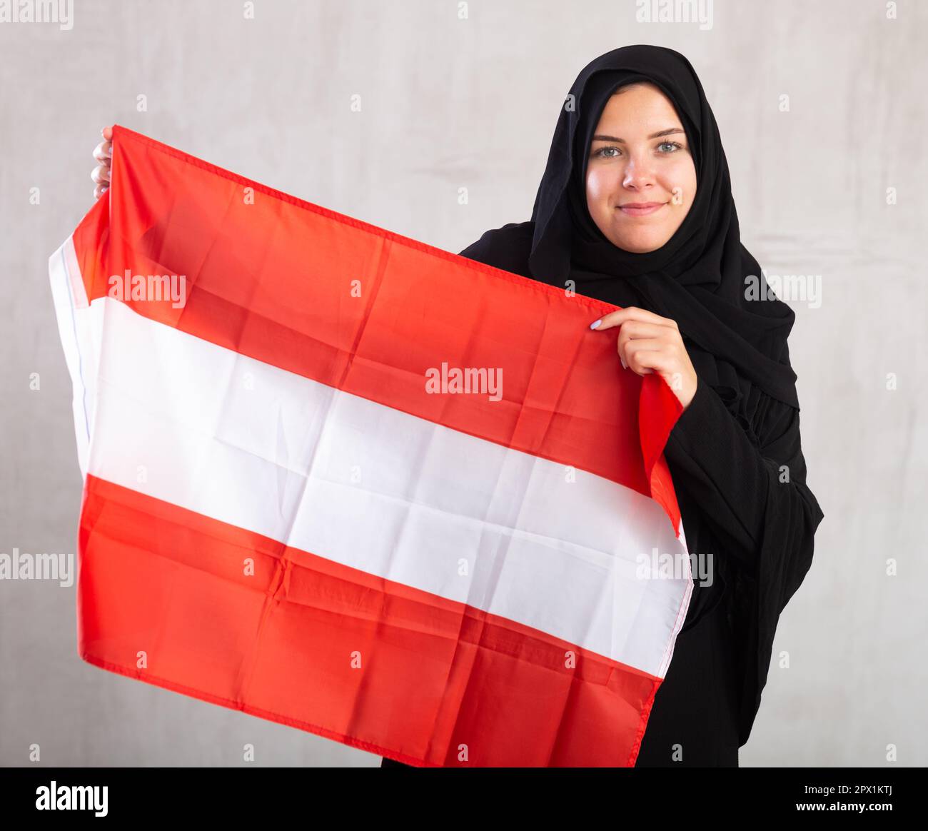 smiling Muslim woman in traditional black hijab holds flag of Austria ...