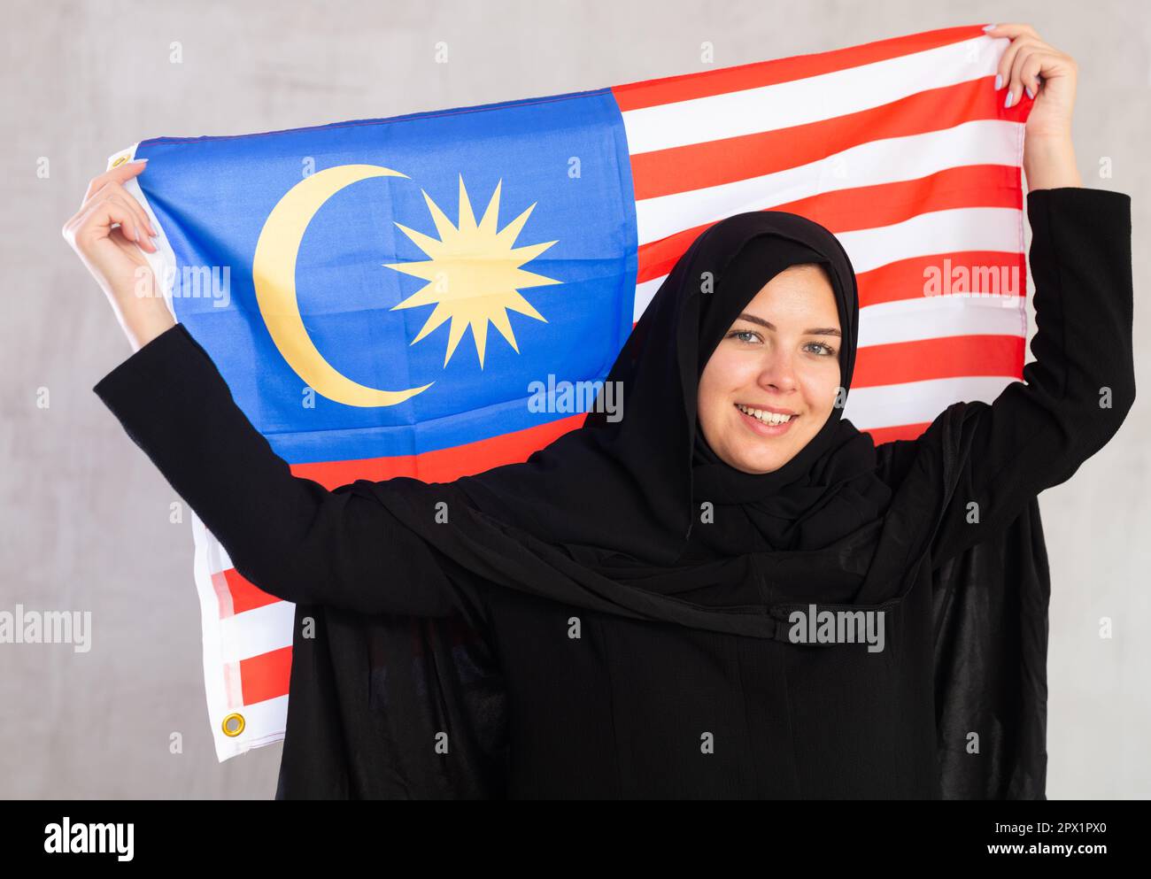 Balanced smiling Muslim woman in traditional black hijab holds flag of ...