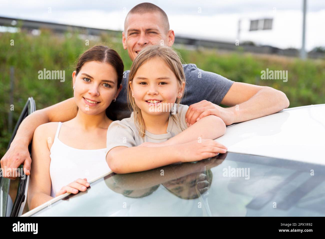 Positive family standing near an open car Stock Photo - Alamy