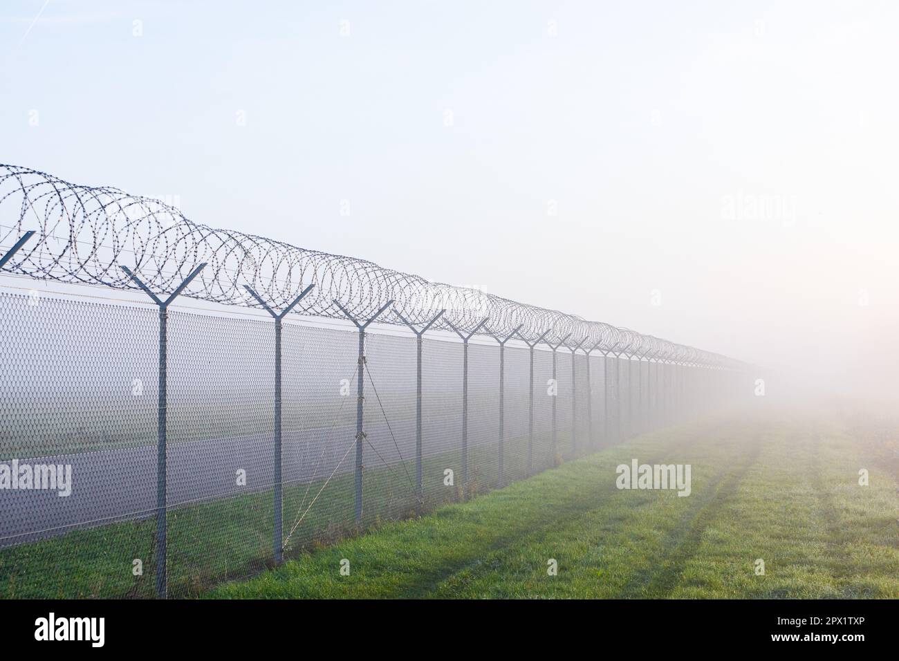 endless long border fence with barbed wire in mist Stock Photo - Alamy