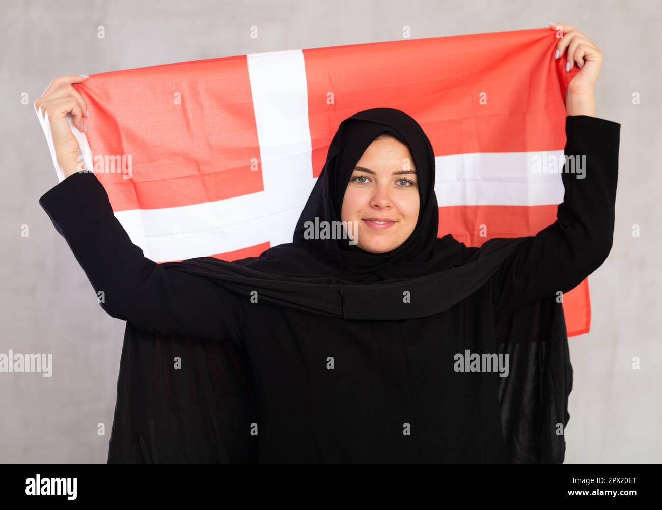 Balanced smiling Muslim woman in traditional black hijab holds flag of ...