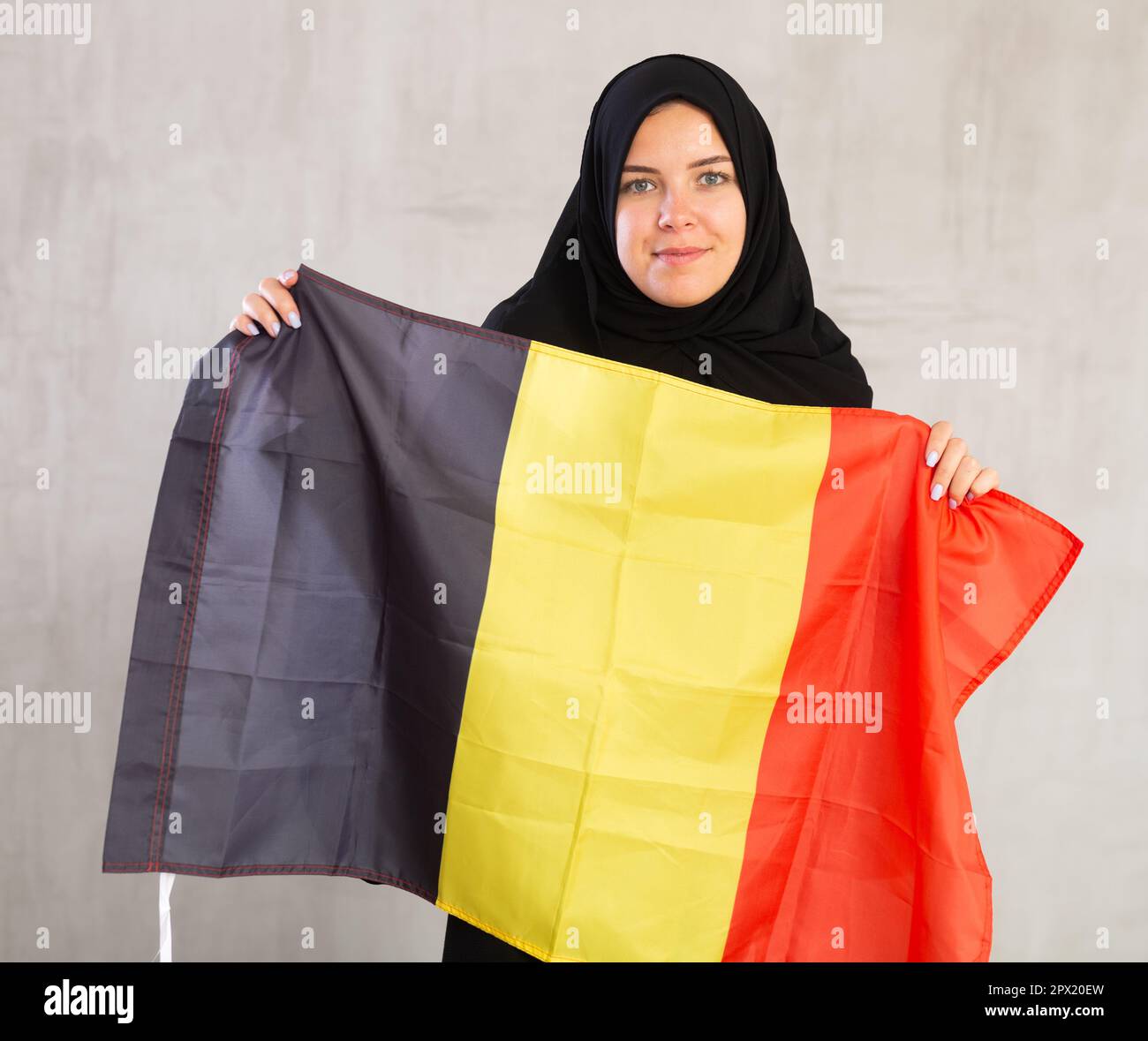 Balanced Muslim woman in traditional black hijab holds flag of Belgium ...