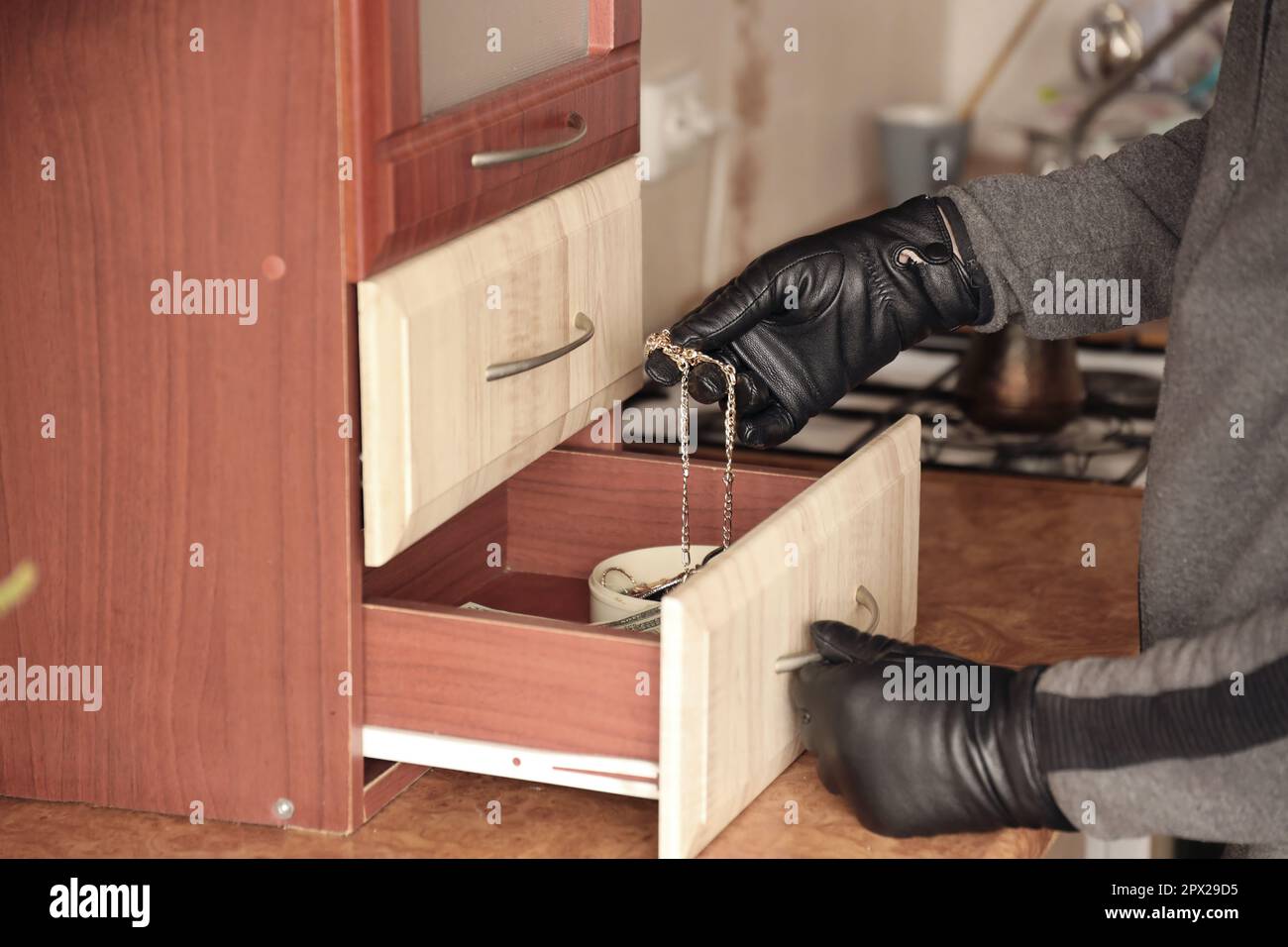 Robber in black outfit and gloves see in opened shelf in kitchen. The ...