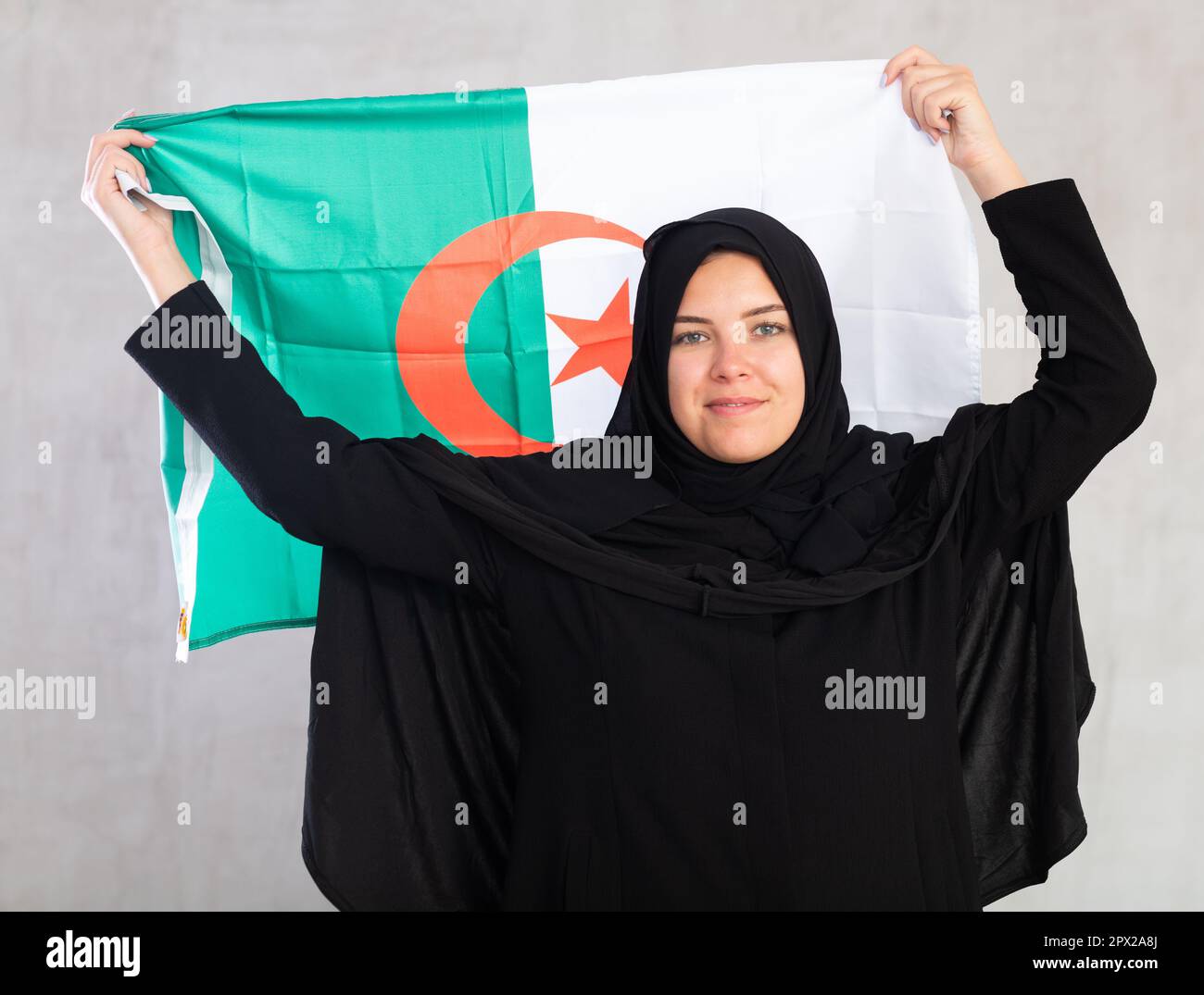 Balanced Muslim woman in traditional black hijab holds flag of Algeria ...