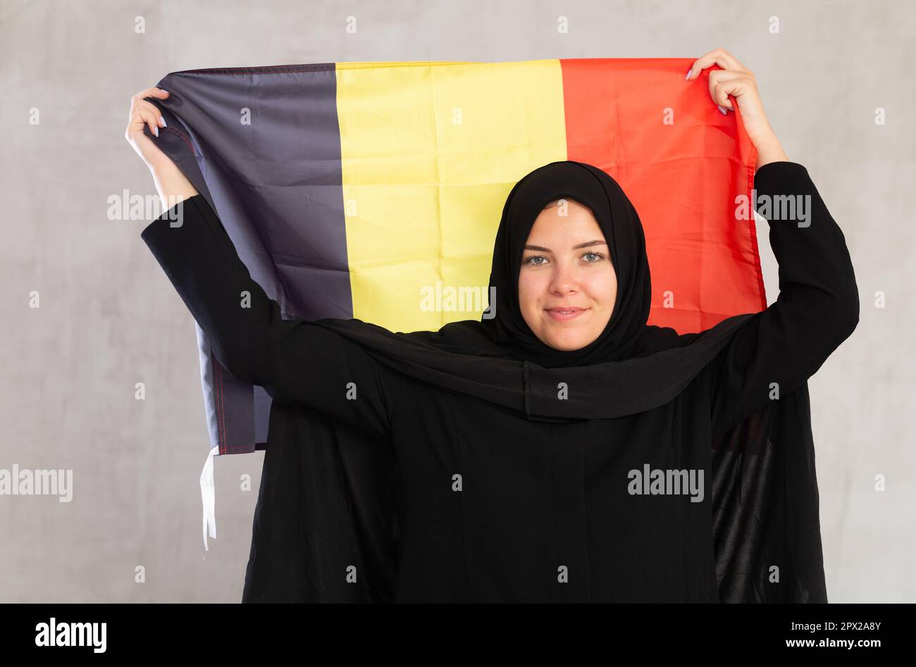 Balanced Muslim woman in traditional black hijab holds flag of Belgium ...
