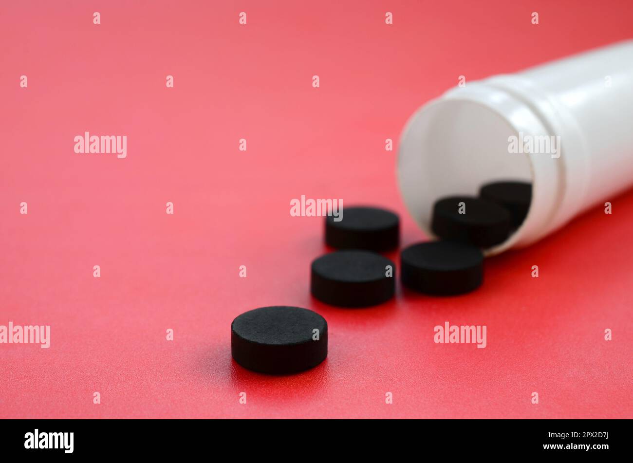 Several black tablets fall out of the plastic jar on the red surface ...