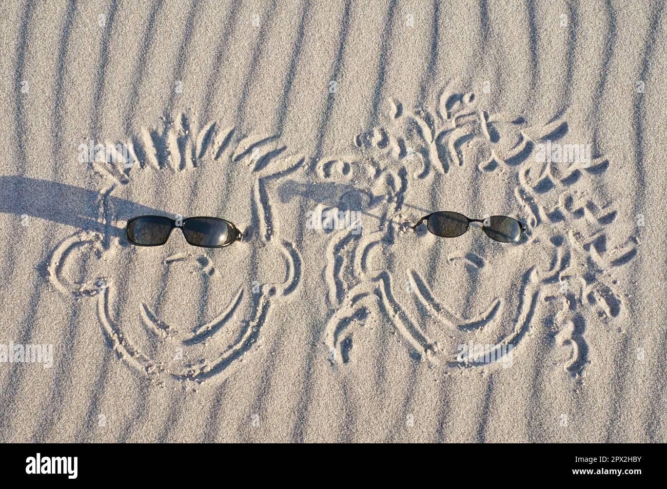 Face drawn in the sand on the beach, with sunglasses. Sand with wave ...