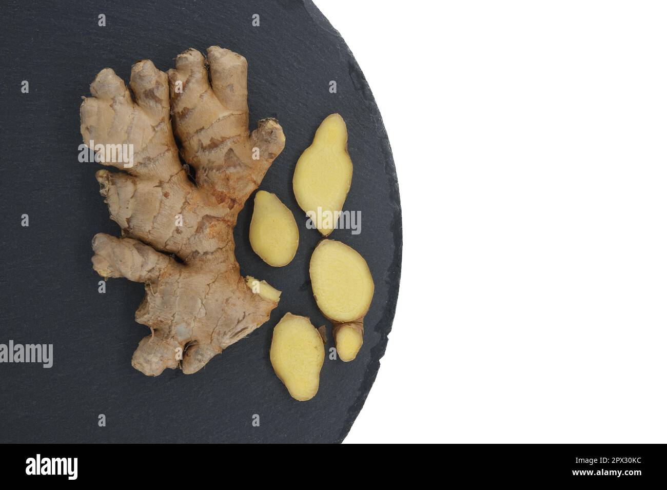 Ginger rhizome with slices on round stone slate coaster. Top view with ...
