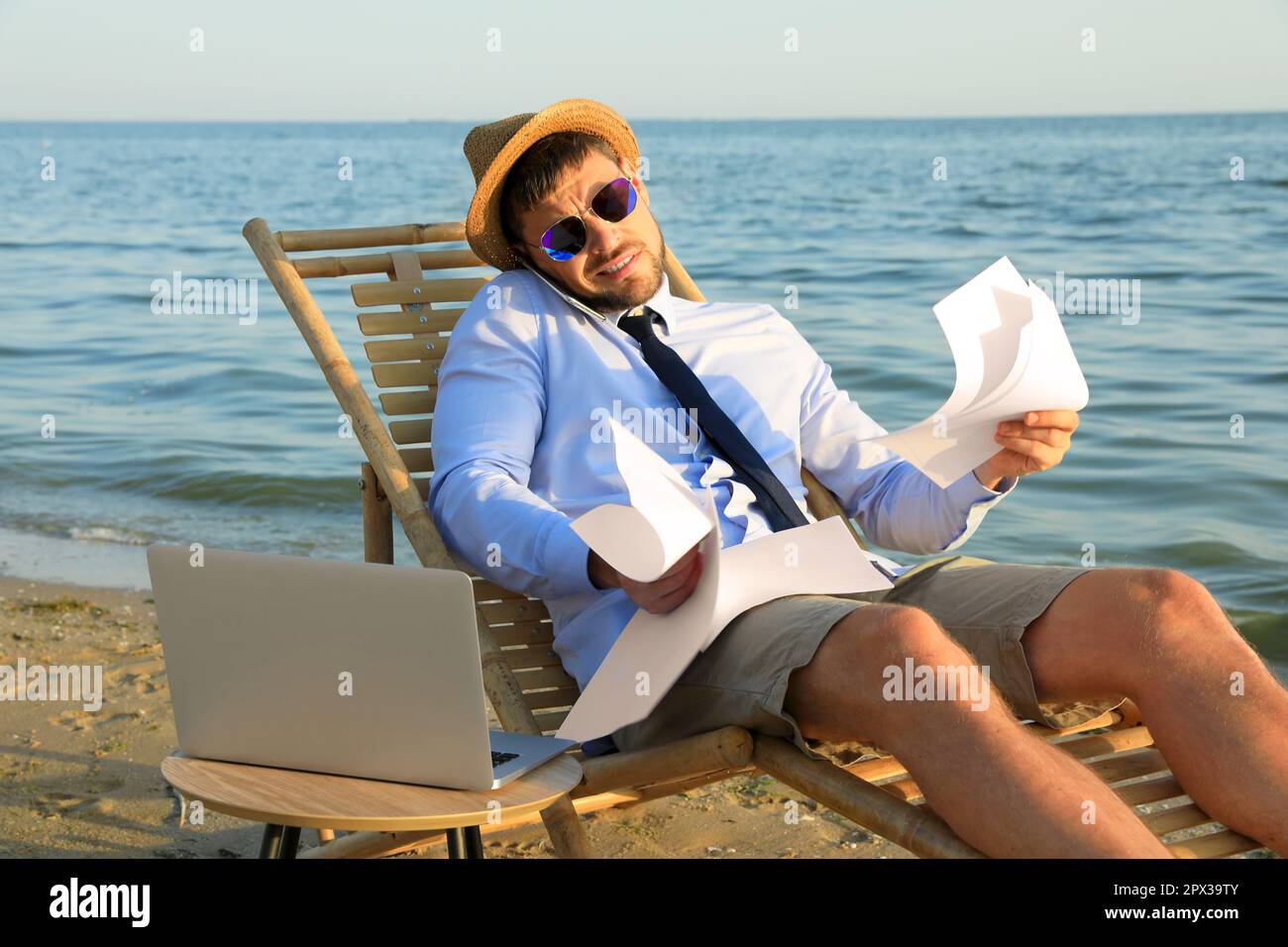 Busy man with papers talking by mobile phone on beach. Business trip ...