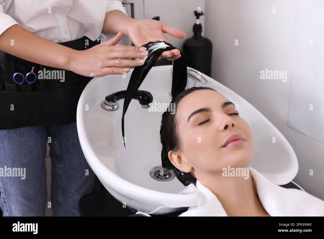 Professional hairdresser applying conditioner on woman's hair in beauty ...