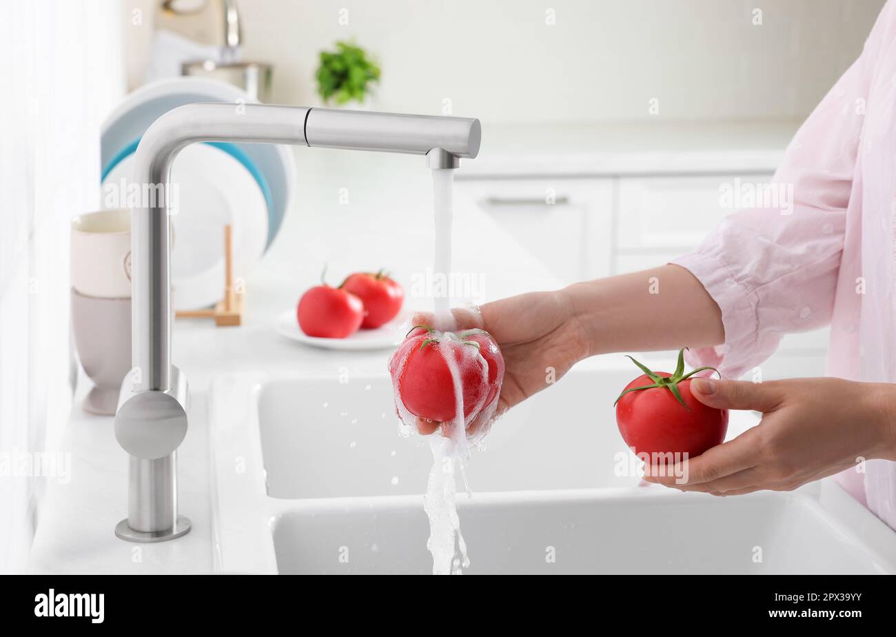 Woman washing fresh ripe tomatoes under tap water in kitchen, closeup ...