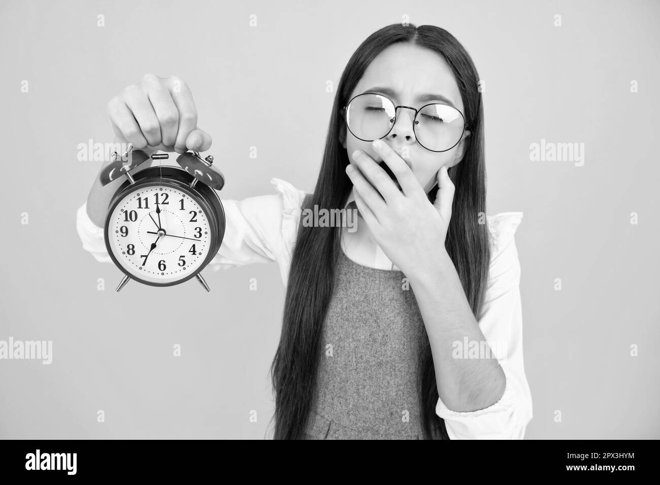 Tired and bored teenager student girl hold clock isolated on yellow ...