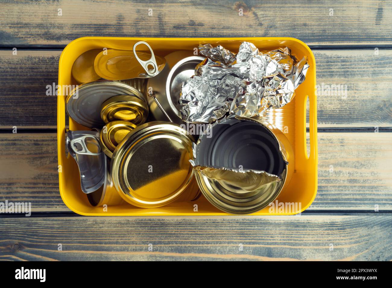 Yellow plastic box with metal canned caps, foil waste on wooden table ...