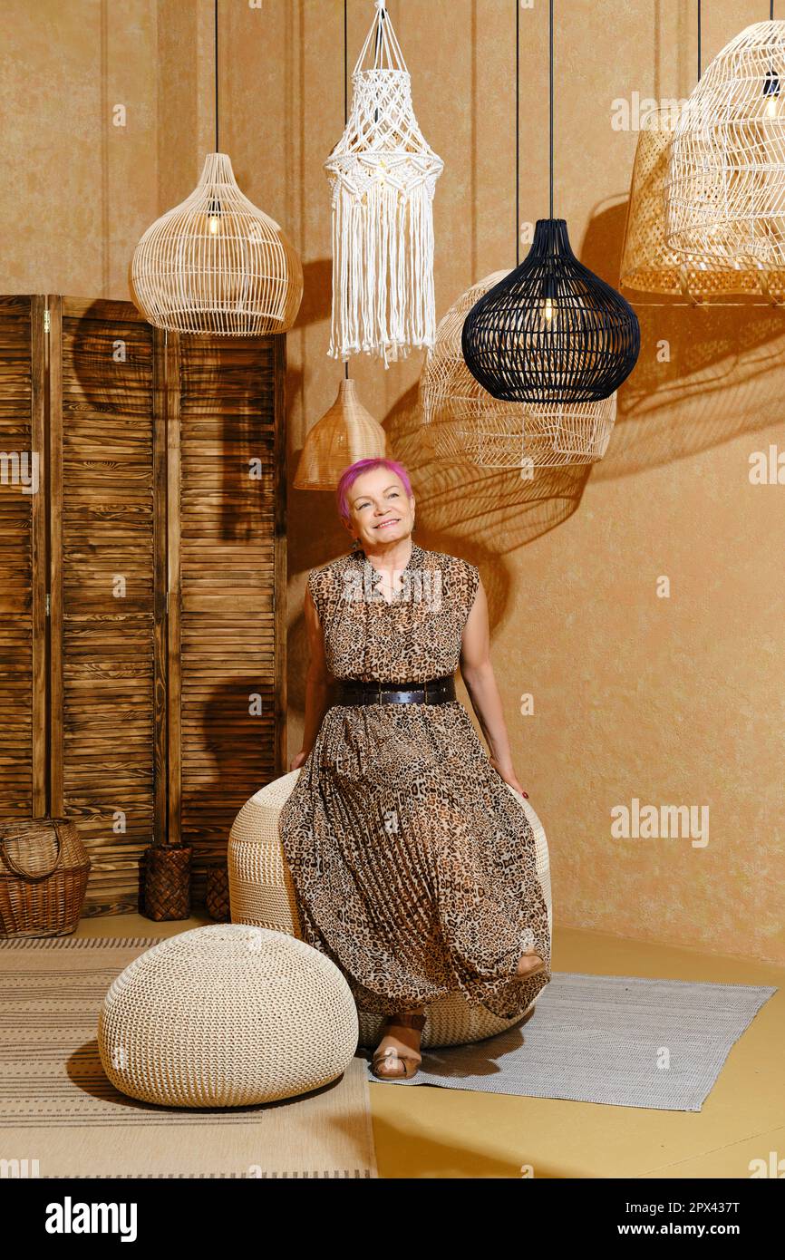 Cheerful and careless old woman with pink hair sitting on wicker padded ...