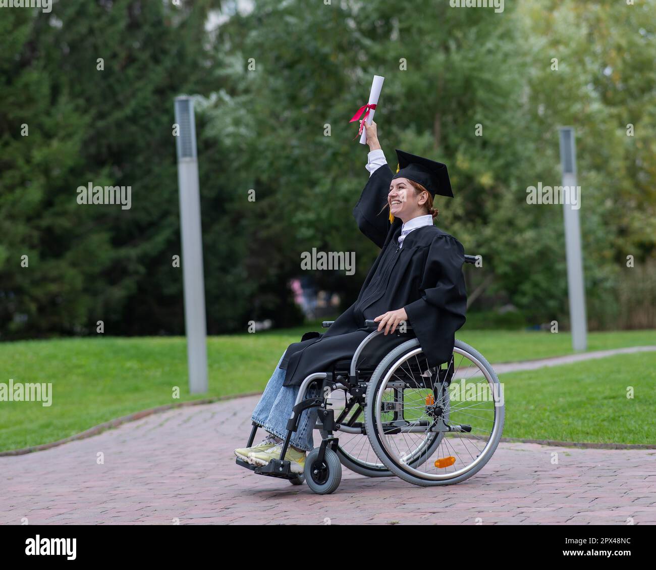 Caucasian woman in a wheelchair in a graduate costume rejoices at ...