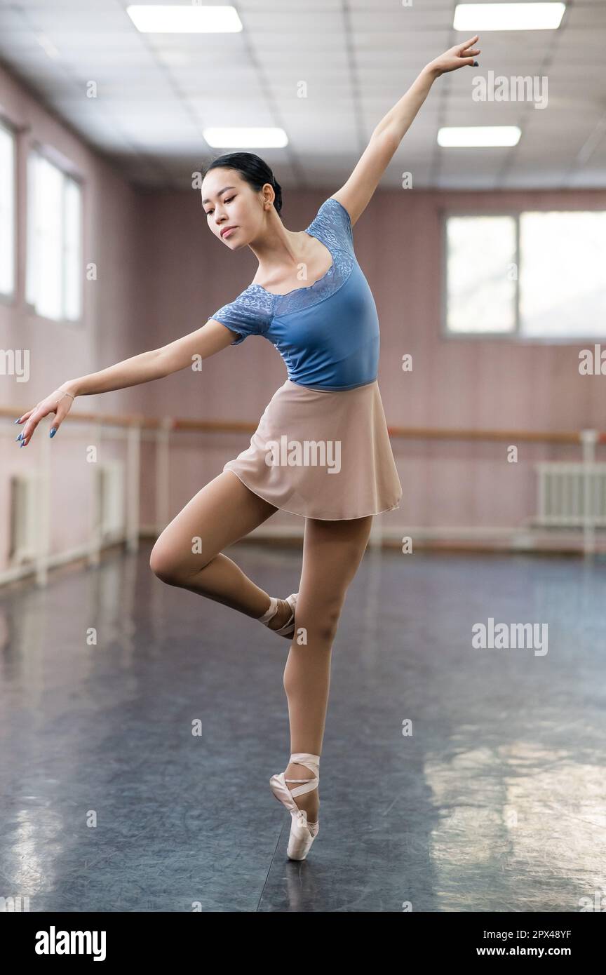 Graceful Asian ballerina in a blue bodysuit and a beige skirt is ...