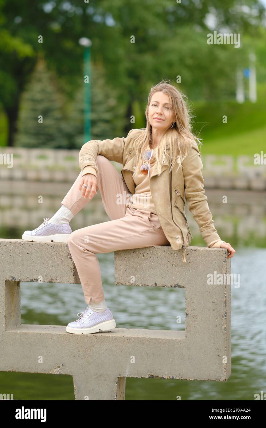 Urban portrait of beautiful active middle aged woman sitting on a fence ...