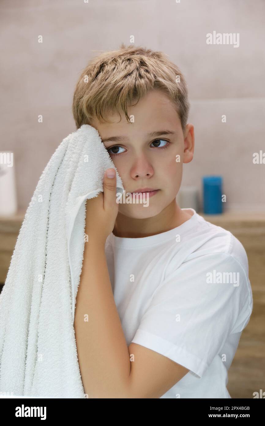 Reflection of a schoolboy wiping his face with a towel after washing in ...