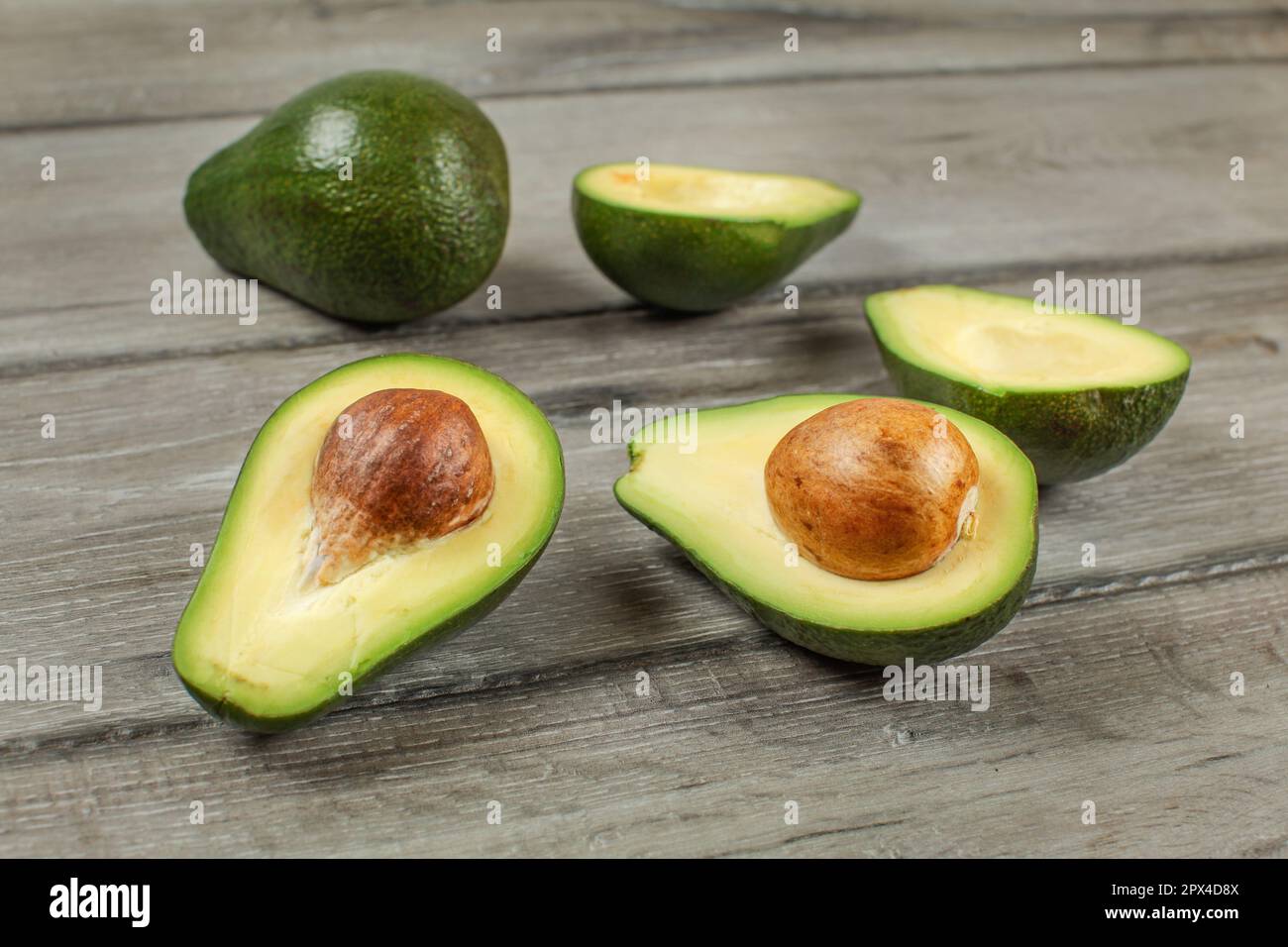 Avocados cut in half seed visible, one whole green pear in background ...