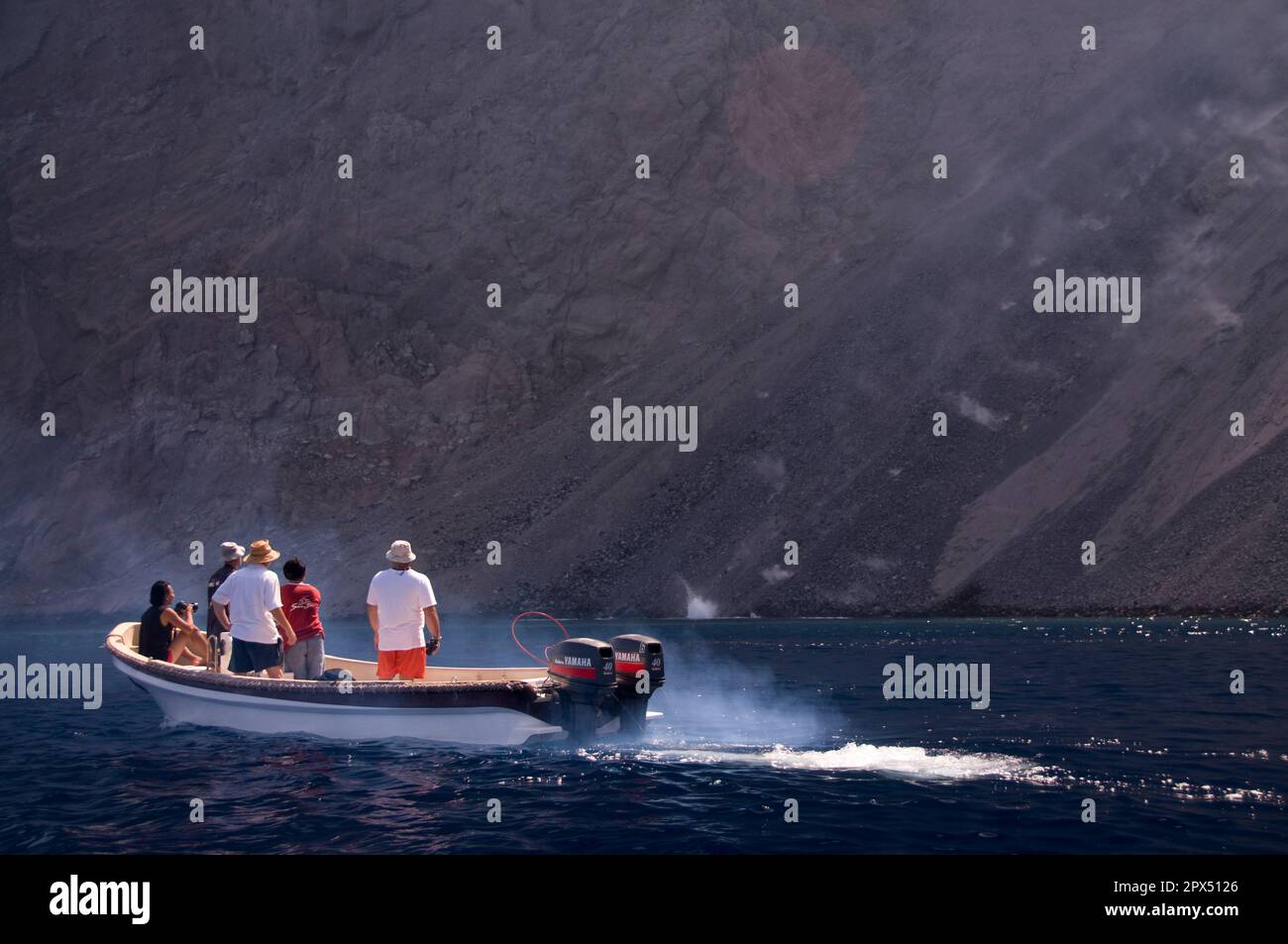 People in small boat watching volcano with smoking fumerole and rocks ...