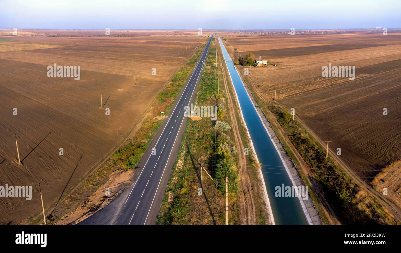 Long asphalt Road with blue water canal, fields aside. Beautiful nature ...
