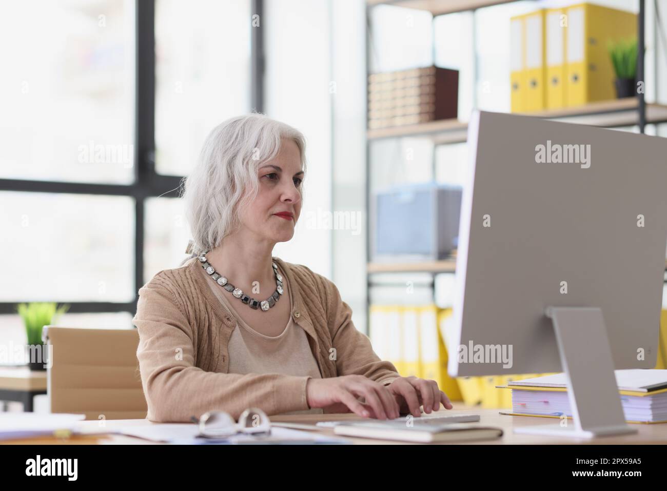 Woman with grey hair looks at screen of computer monitor Stock Photo ...