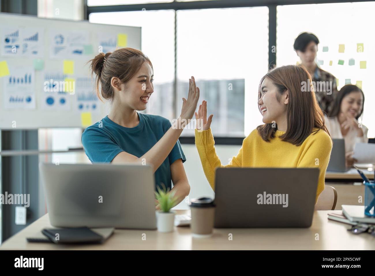 Young asian woman with modern laptop giving five to colleague partner in front after completed ...
