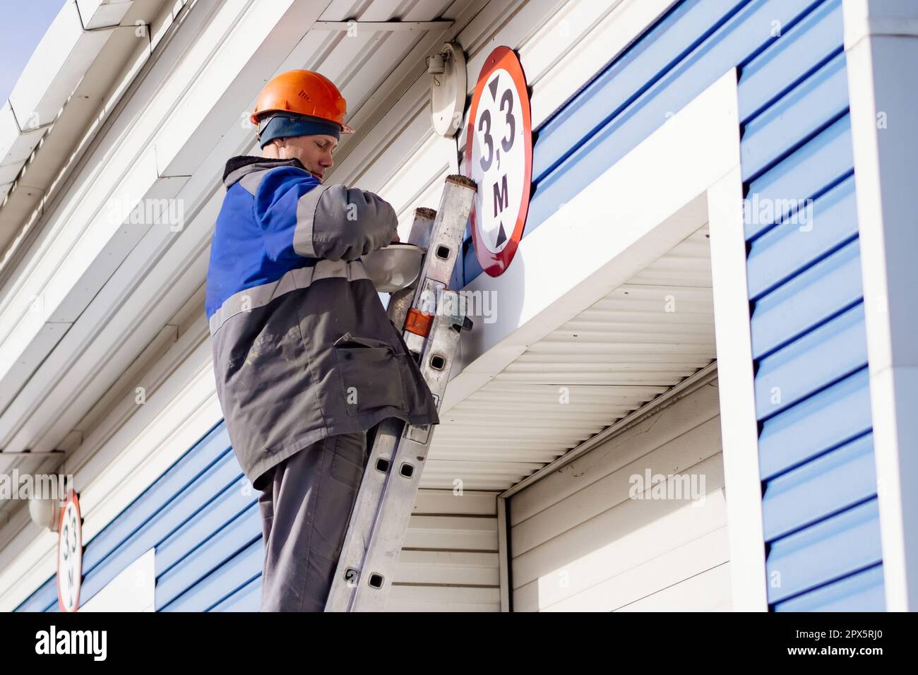 Male electrician stands on ladder and replaces light bulb in ceiling ...