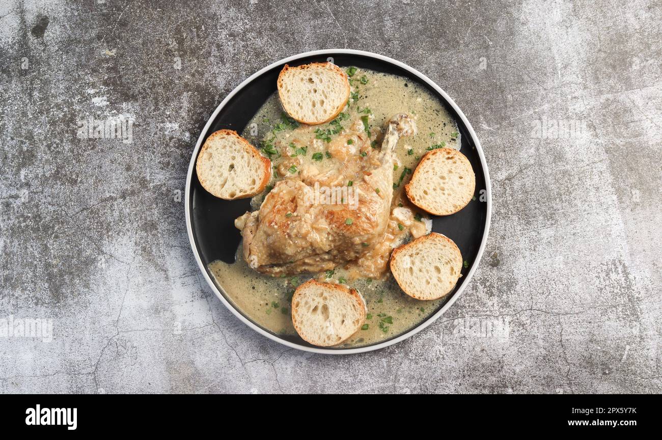 Stewed chicken leg with garlic and bread on a round plate on a dark ...