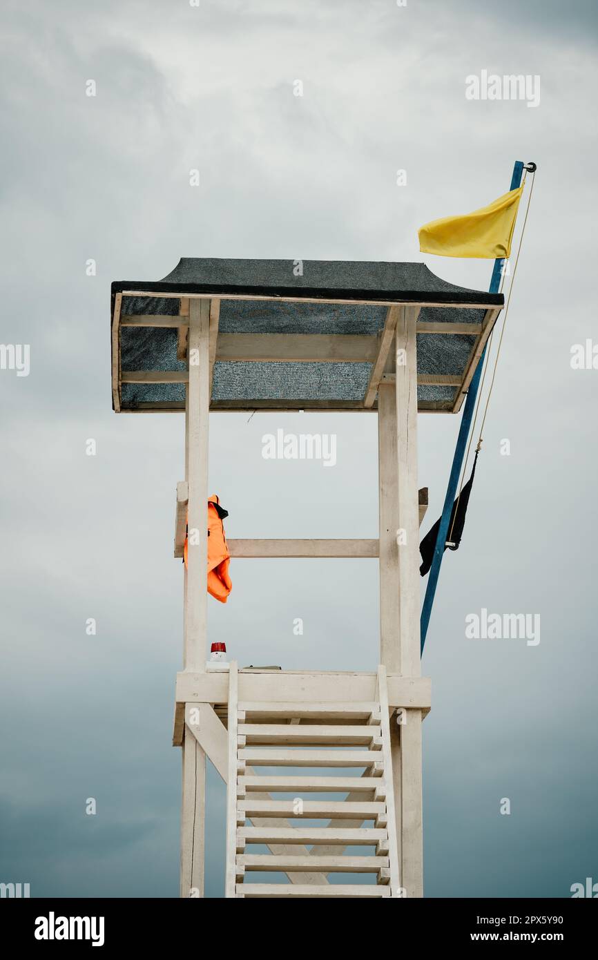 Empty white lifeguard tower with a yellow flag on the beach in windy ...