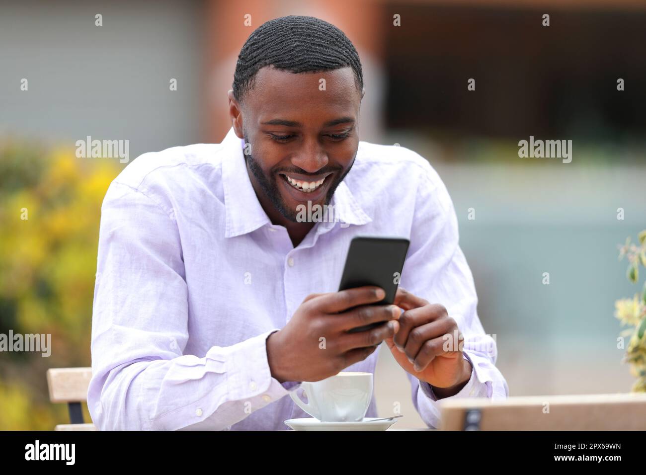 Happy black man checking mobile phone sititng in a bar terrace Stock ...