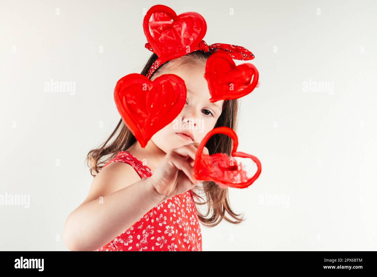 Pretty little girl carefully draw red hearts with paintbrush on ...