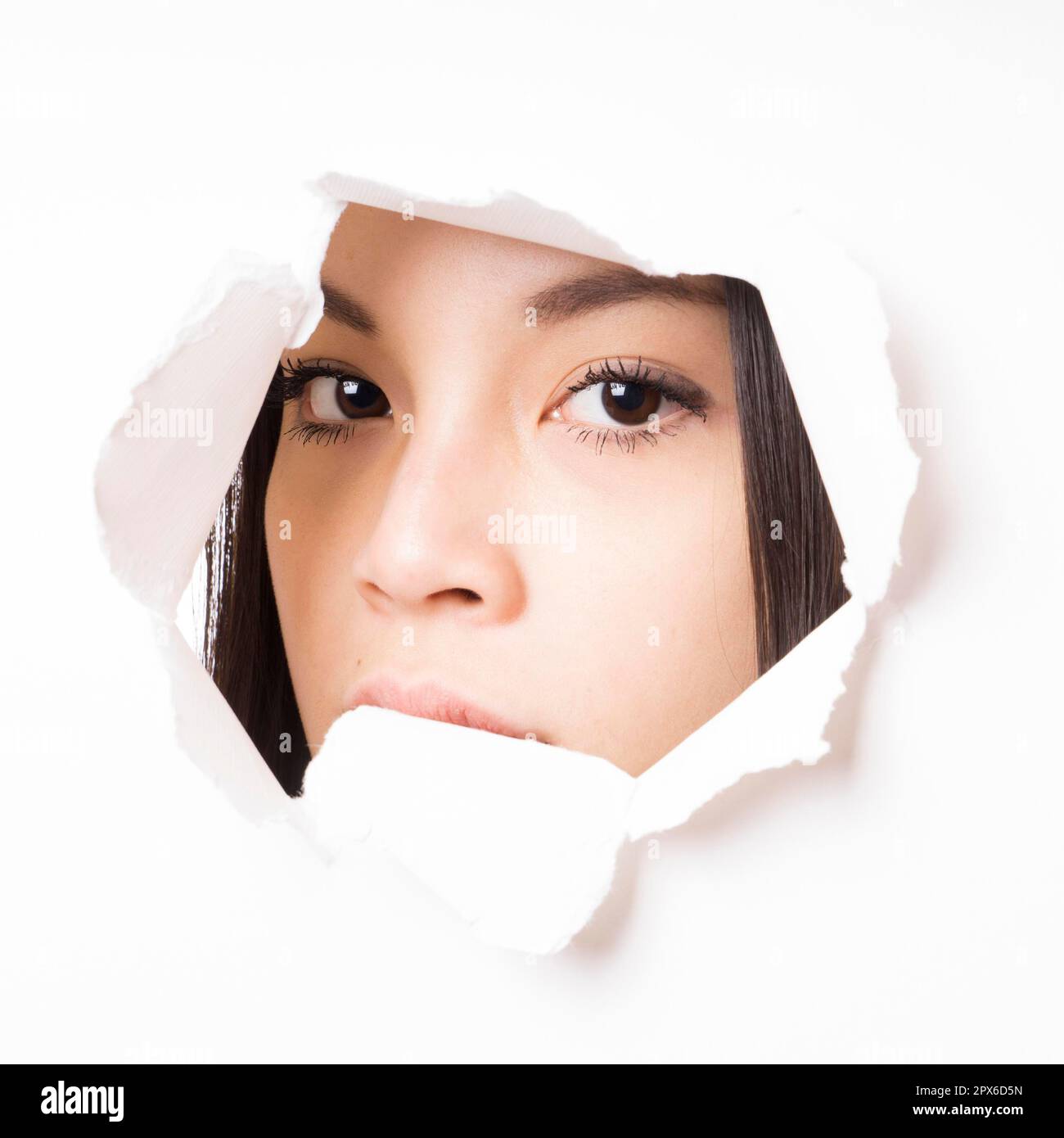 young asian woman peeking through hole torn in paper wall Stock Photo ...