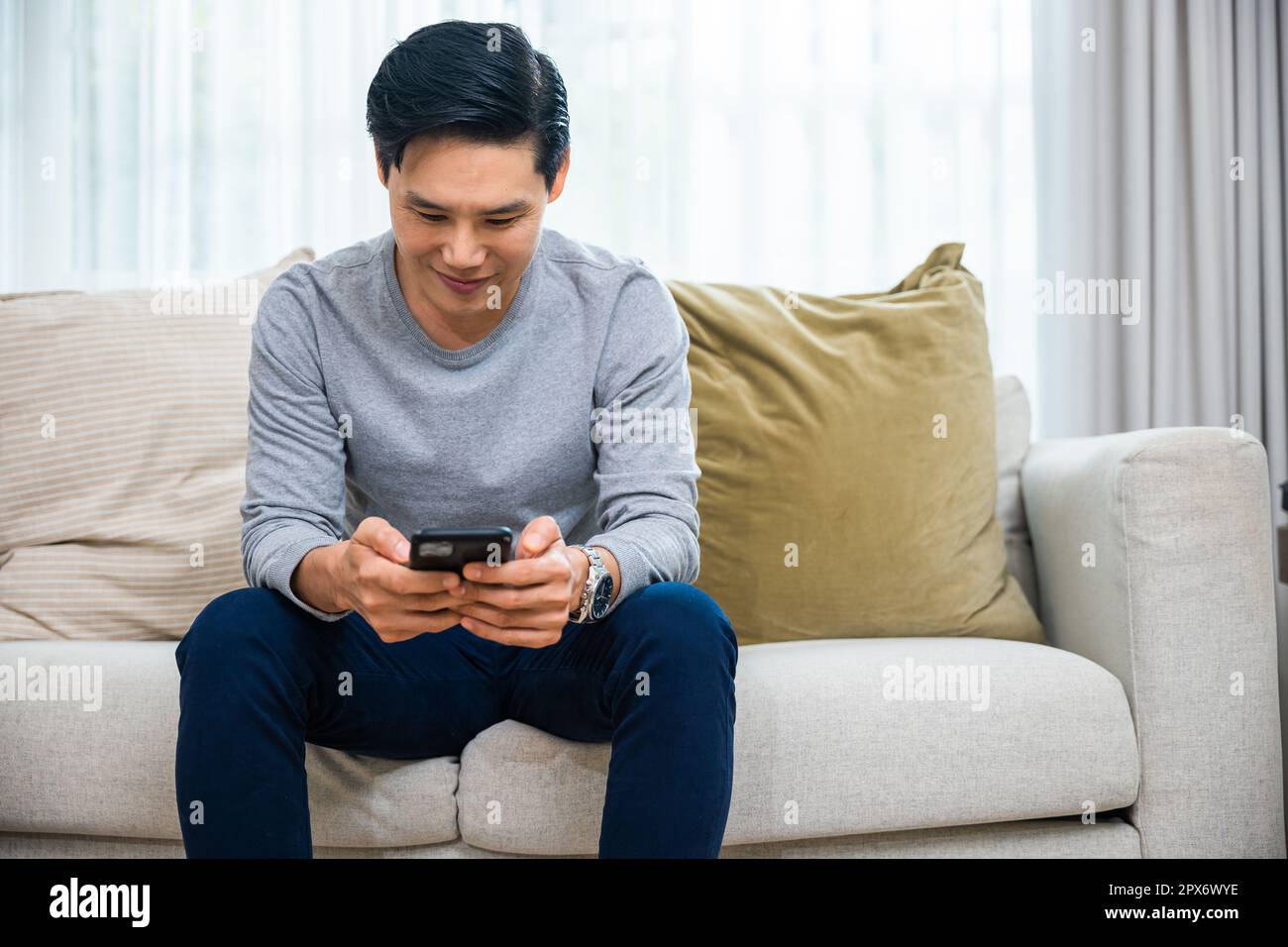 Asian older middle aged man relaxing sitting on sofa using smart mobile ...